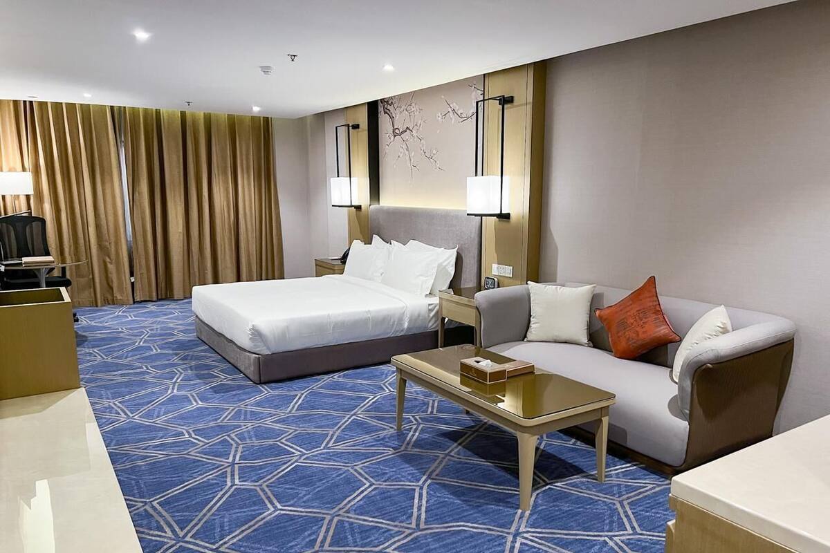 Quarto de hotel com uma cama grande, um sofá, uma mesa de centro e um tapete estampado.