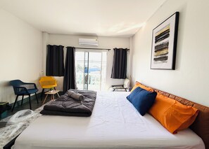 Quarto de hotel com cama, cadeira, mesa pequena com planta e janela com cortinas.