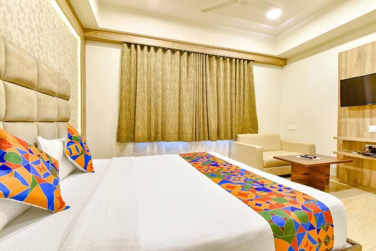 Quarto de hotel com uma cama grande, um sofá, uma mesinha e uma TV fixada na parede.