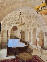 Quarto com parede de pedra, cama, lustre e mesa com cadeiras.
