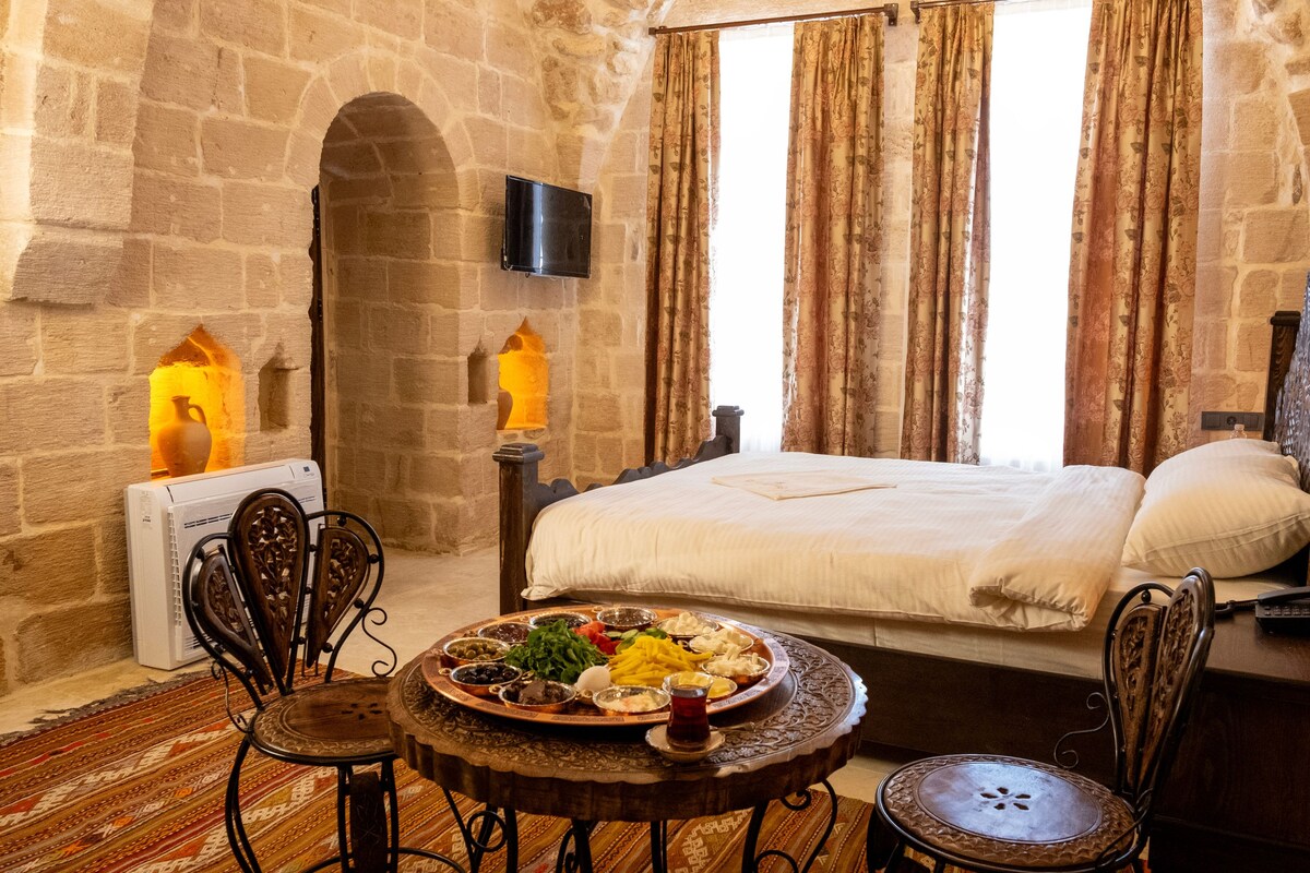 Quarto tradicional com paredes de pedra, uma cama, uma mesa com comida e uma televisão.