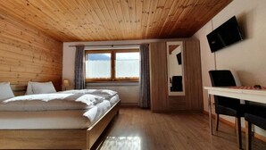 Quarto com teto de madeira, uma cama, uma escrivaninha e uma televisão na parede.