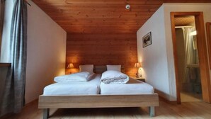Quarto com painéis de madeira, uma cama, duas luminárias de cabeceira e uma porta que dá para outro espaço.