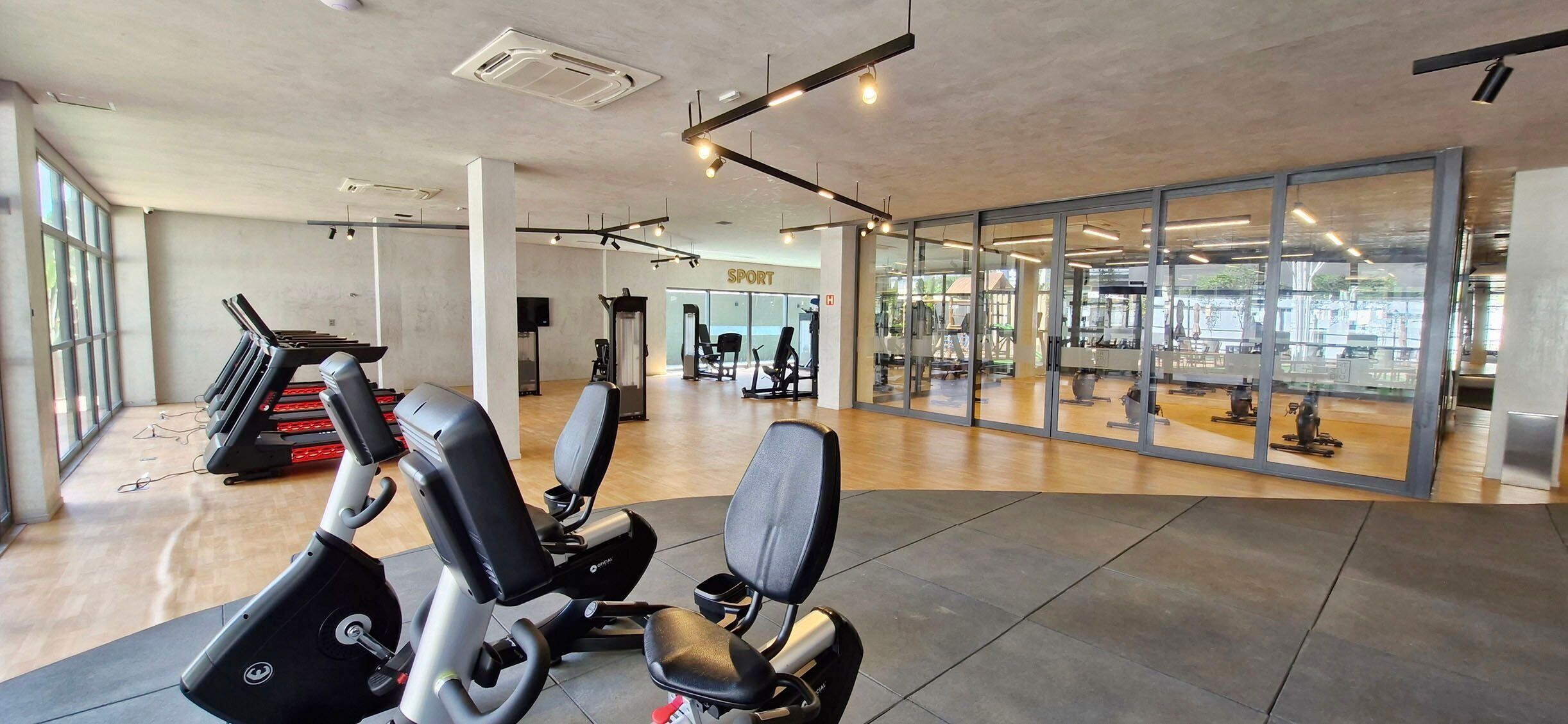 Uma academia com equipamentos de ginástica, um banco de musculação e uma parede com grandes janelas.