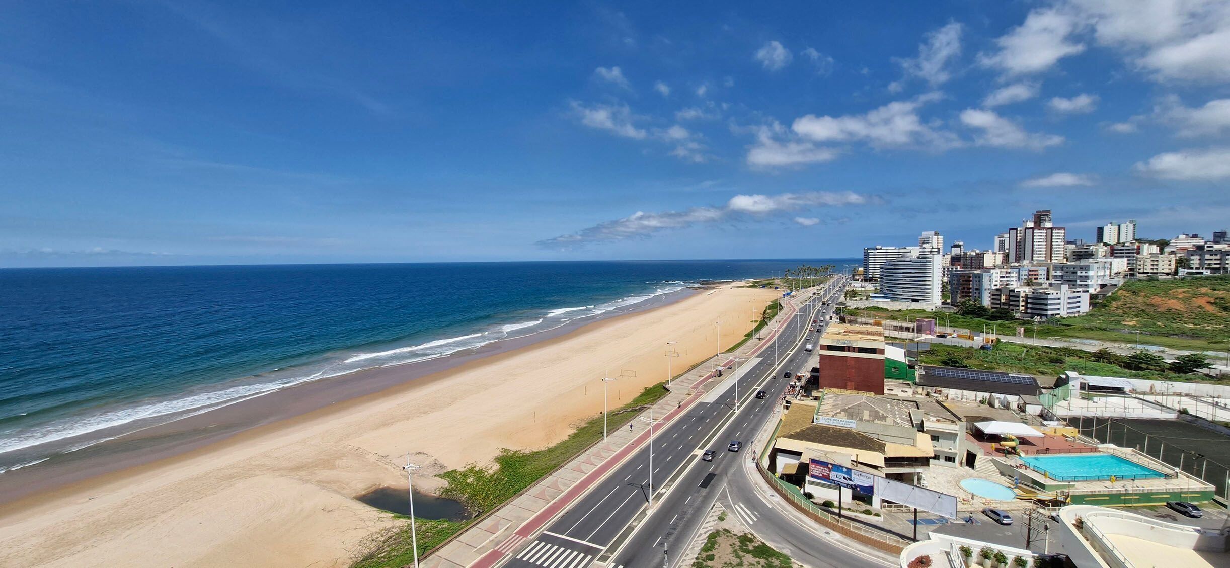 Paisagem costeira com praia, uma estrada ao longo da orla e edifícios altos.