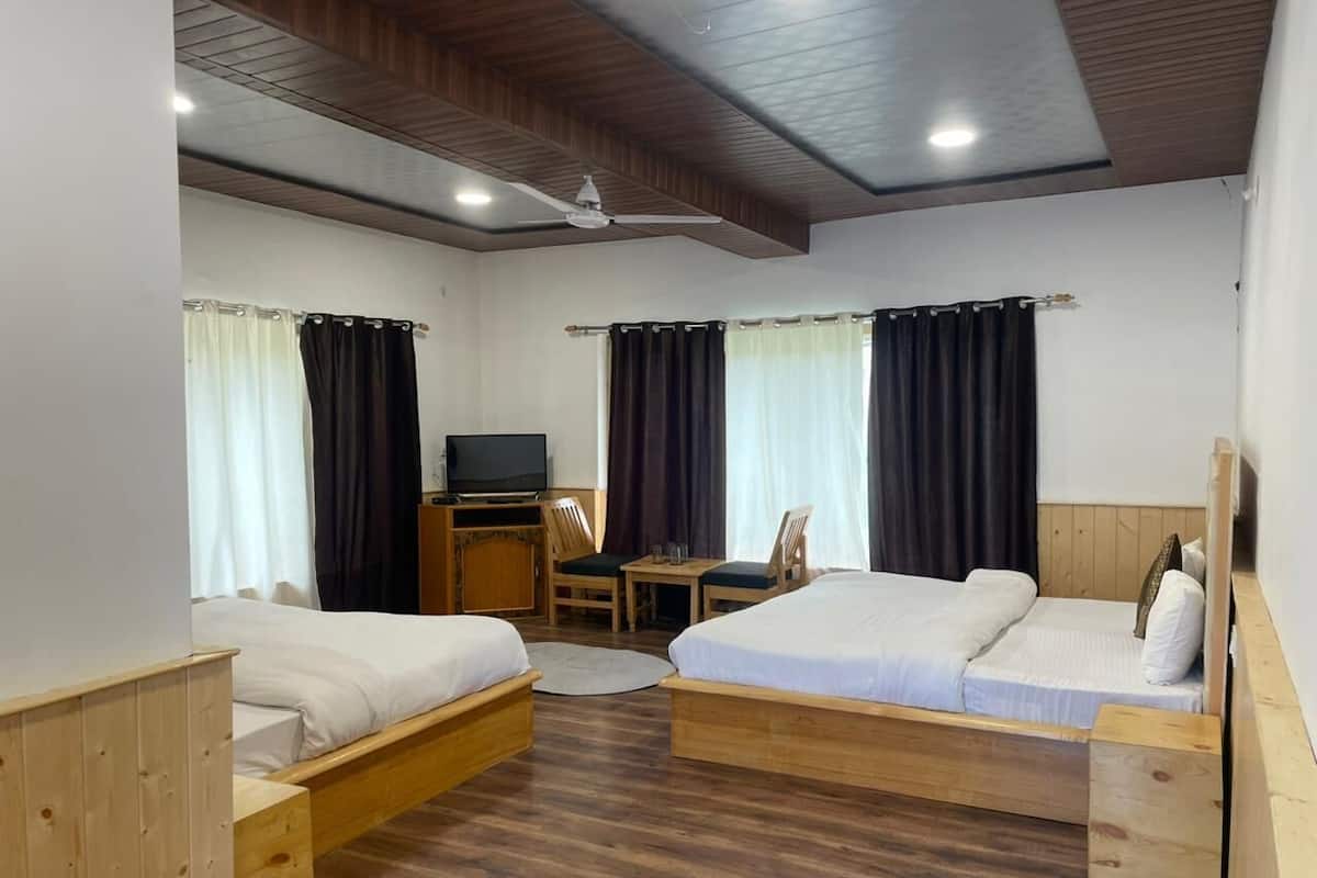 Quarto de hotel com duas camas de solteiro, uma escrivaninha com cadeira, televisão e piso de madeira.