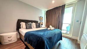 Quarto com cama, mesa de cabeceira e vista para o exterior.