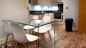 Uma cozinha moderna com mesa de jantar de vidro, cadeiras brancas e um vaso com flores.
