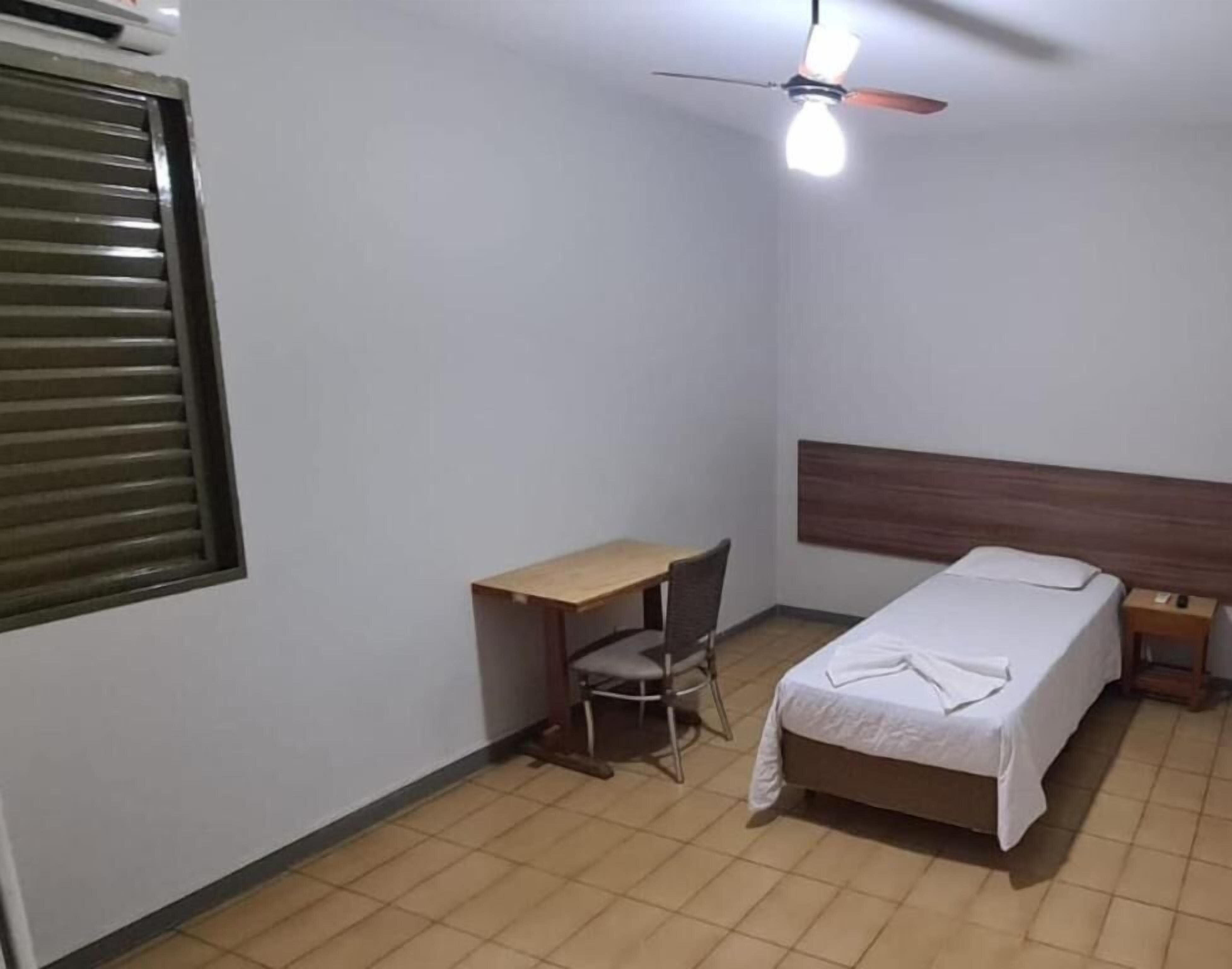 Um quarto pequeno e limpo, com uma cama, uma escrivaninha e uma cadeira.