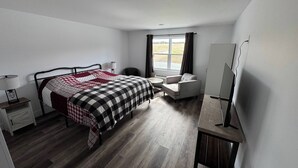 Um quarto com uma cama, uma cadeira, uma escrivaninha e uma janela com cortinas.