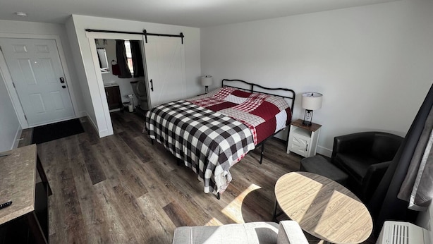 Quarto de hotel pequeno com uma cama, escrivaninha, cadeira, mesa e guarda-roupa.