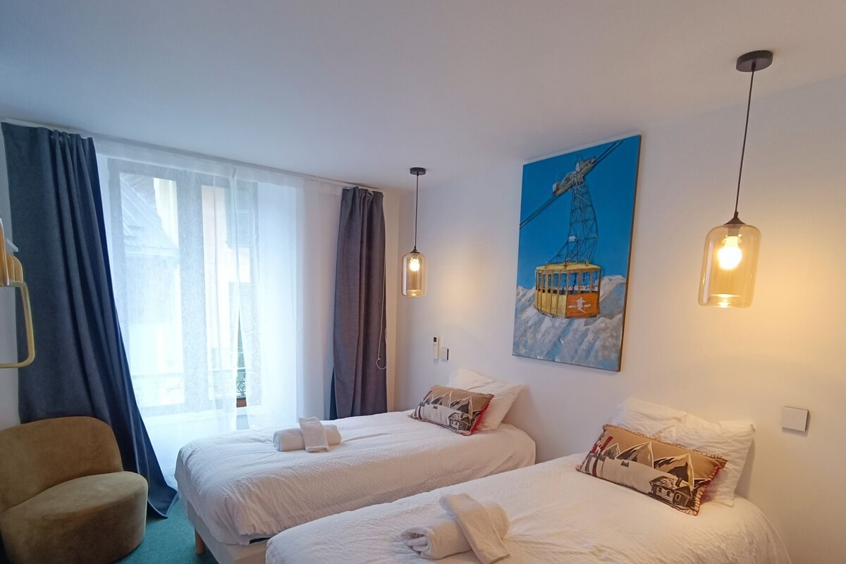 Quarto de hotel com duas camas, uma cadeira, um quadro e uma luminária no teto.