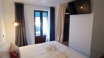 Quarto de hotel com uma cama grande, televisão fixada na parede, janela com cortinas e vista para o exterior.