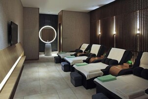 Sala de spa com cadeiras de massagem, uma TV e um lustre circular.