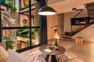 Uma sala de estar moderna com uma janela grande, uma mesa redonda com uma garrafa e copos, e uma escada com corrimão de metal.