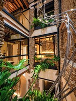 Interior com vários níveis, paredes de pedra, janelas amplas e plantas.