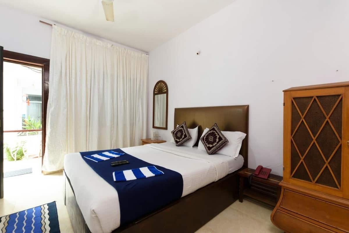 Quarto de hotel com cama, guarda-roupa de madeira, mesa de cabeceira, espelho e janela com cortinas.