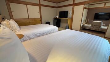 Quarto de hotel com duas camas, uma televisão, uma mesinha e um sofá.