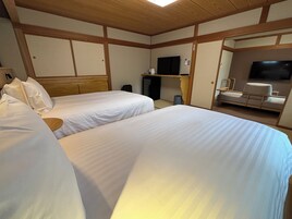 Quarto de hotel com duas camas, uma televisão, uma mesinha e um sofá.