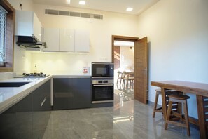 Cozinha moderna com forno embutido, micro-ondas e fogão a gás. Há uma mesa de jantar de madeira com dois banquinhos.