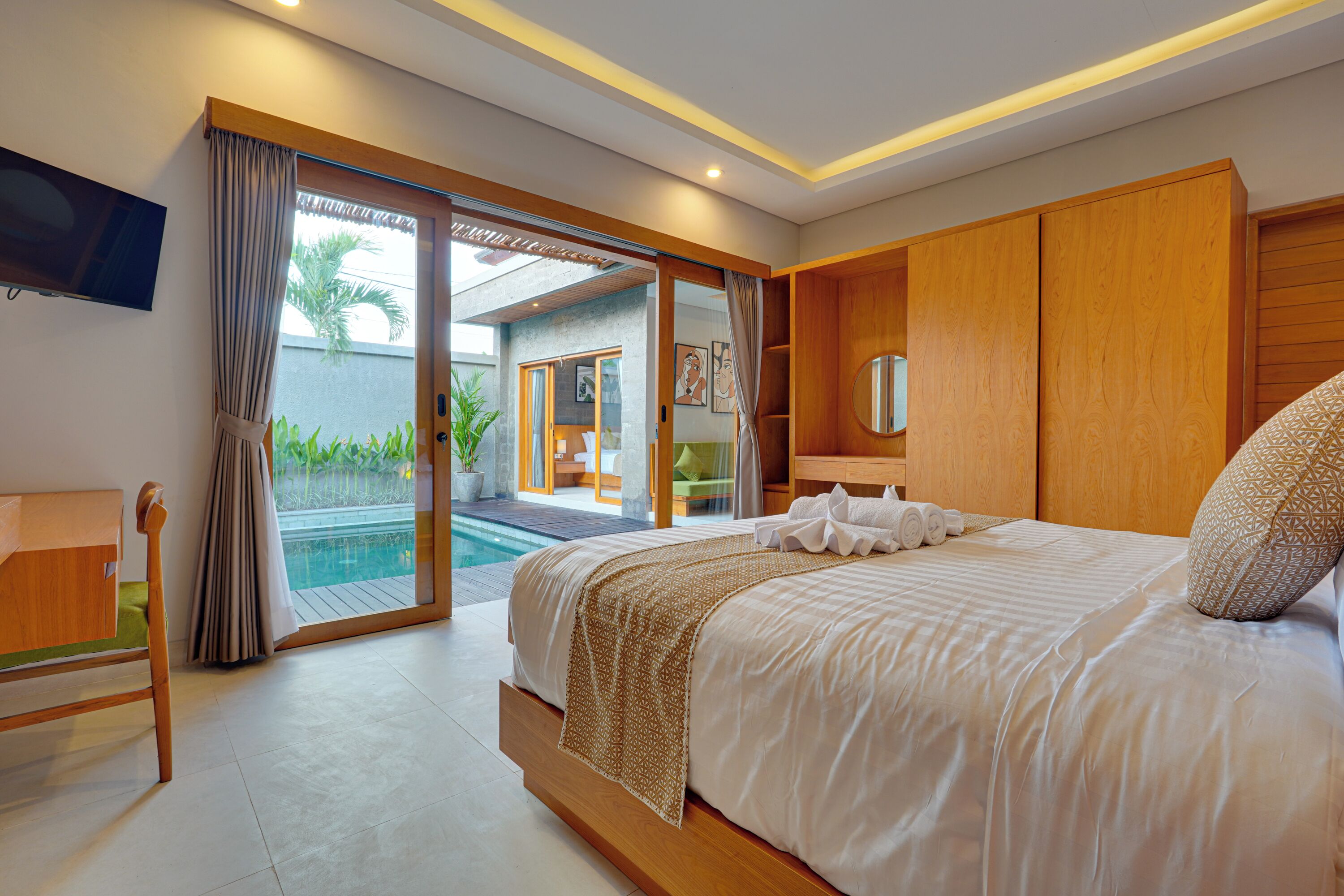 Um quarto moderno com uma cama grande, um guarda-roupa de madeira, uma televisão na parede e uma porta de vidro deslizante para uma área de piscina.