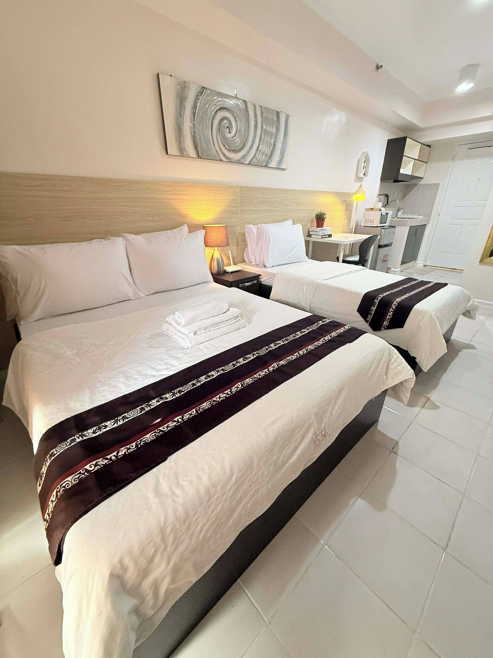 Quarto de hotel com duas camas, uma pequena cozinha e um quadro na parede.