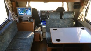 Interior compacto de uma RV com sofá, mesa e televisão.