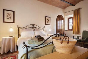 Quarto arrumado com cama, mesas de cabeceira, um cesto de vime e uma cadeira.