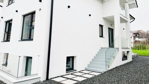 Um edifício moderno de dois andares, com fachada branca, várias janelas e uma escadaria que dá acesso ao andar superior.