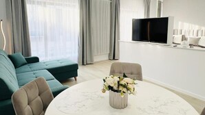 Uma sala de estar moderna com um sofá seccional, uma mesa de centro redonda com um arranjo floral e uma TV de tela plana fixada na parede.