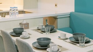 Uma sala de jantar moderna com uma mesa branca posta para dois, uma luminária pendente trançada e detalhes em azul-turquesa nas paredes e nos assentos.
