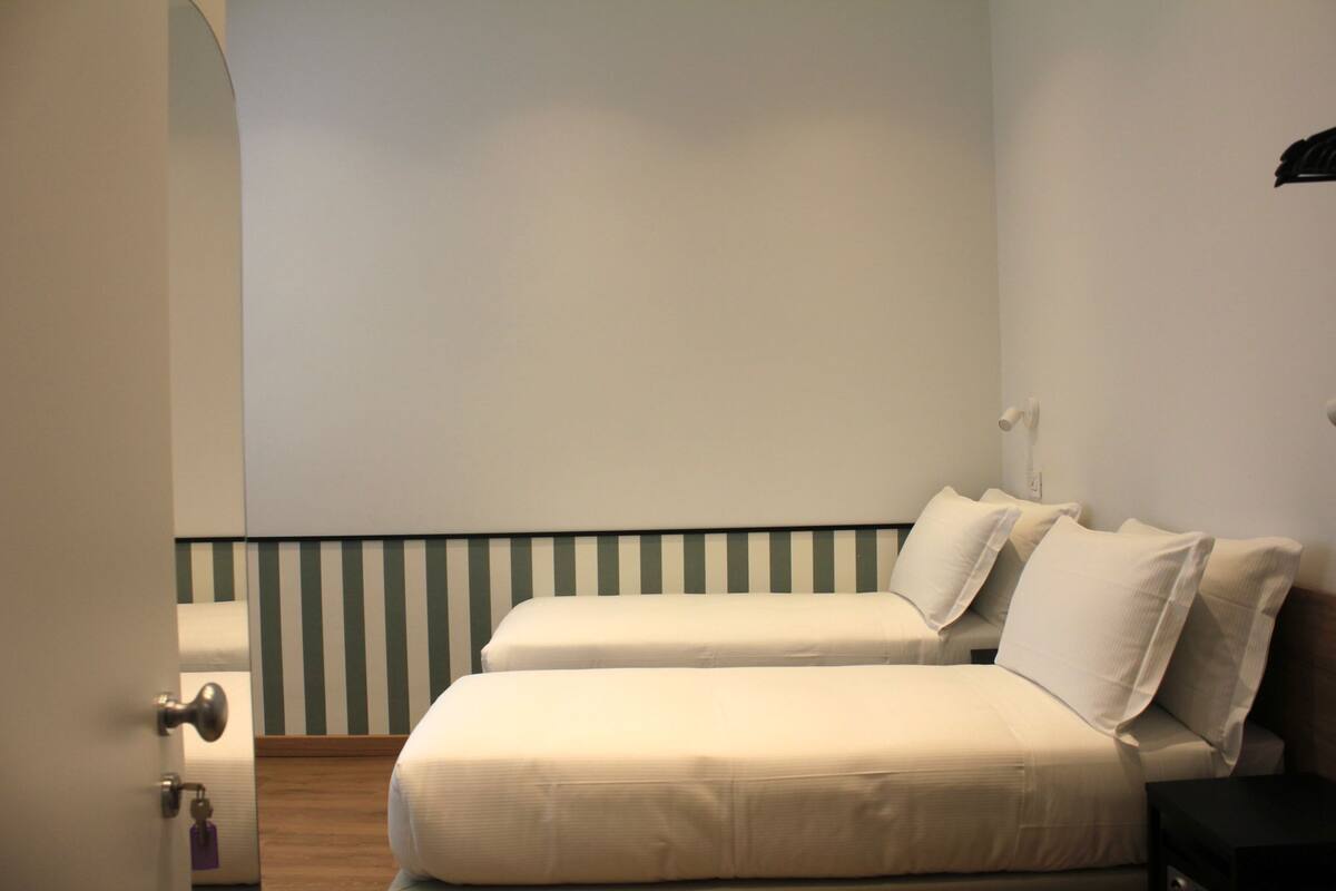 Quarto com duas camas, piso de madeira, parede listrada e porta com maçaneta.