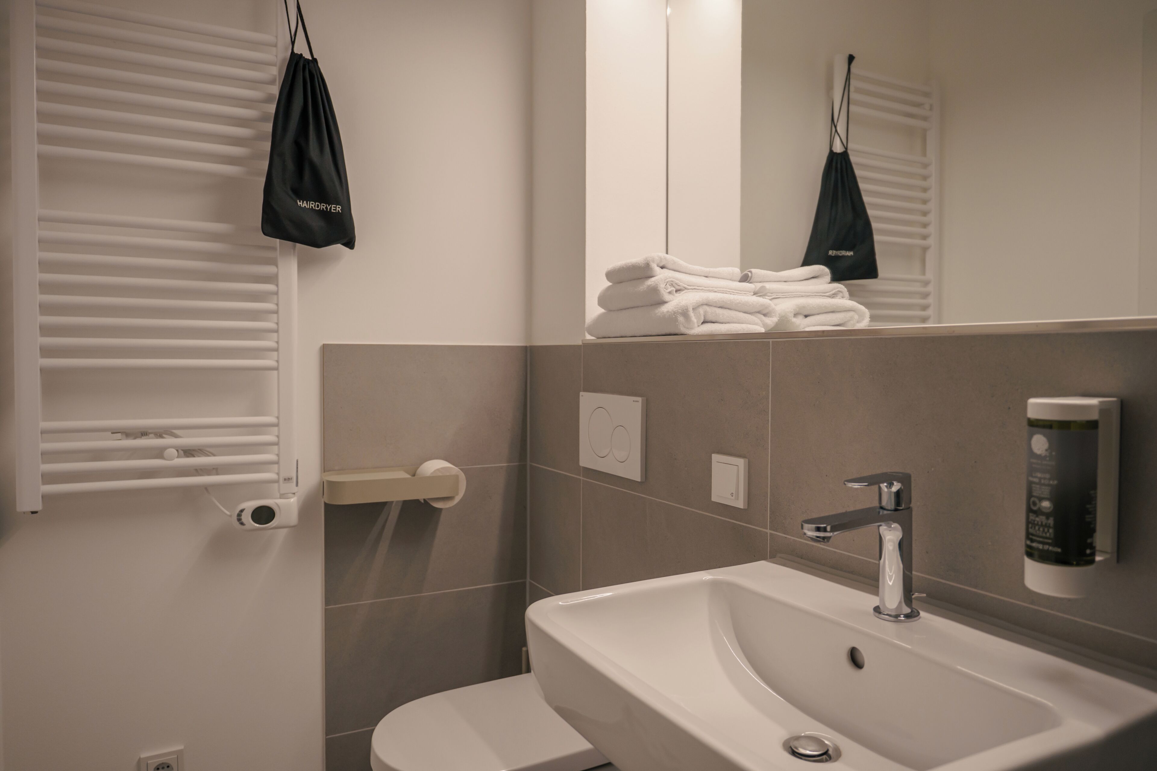 Uma casa de banho moderna com lavatório, sanita, porta-toalhas e saco para secador de cabelo.