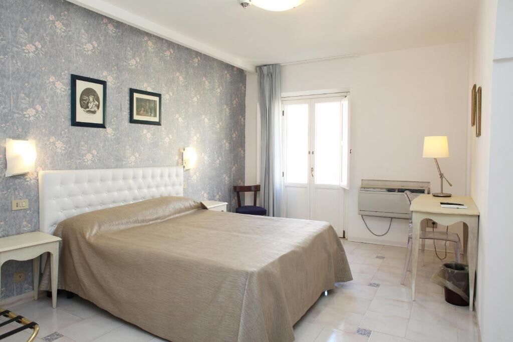 Quarto com uma cama grande, uma escrivaninha com luminária, uma cadeira e um radiador.