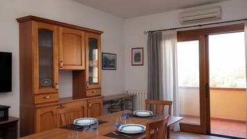 Uma sala de jantar com uma mesa de madeira posta para quatro pessoas, um armário e uma televisão na parede.