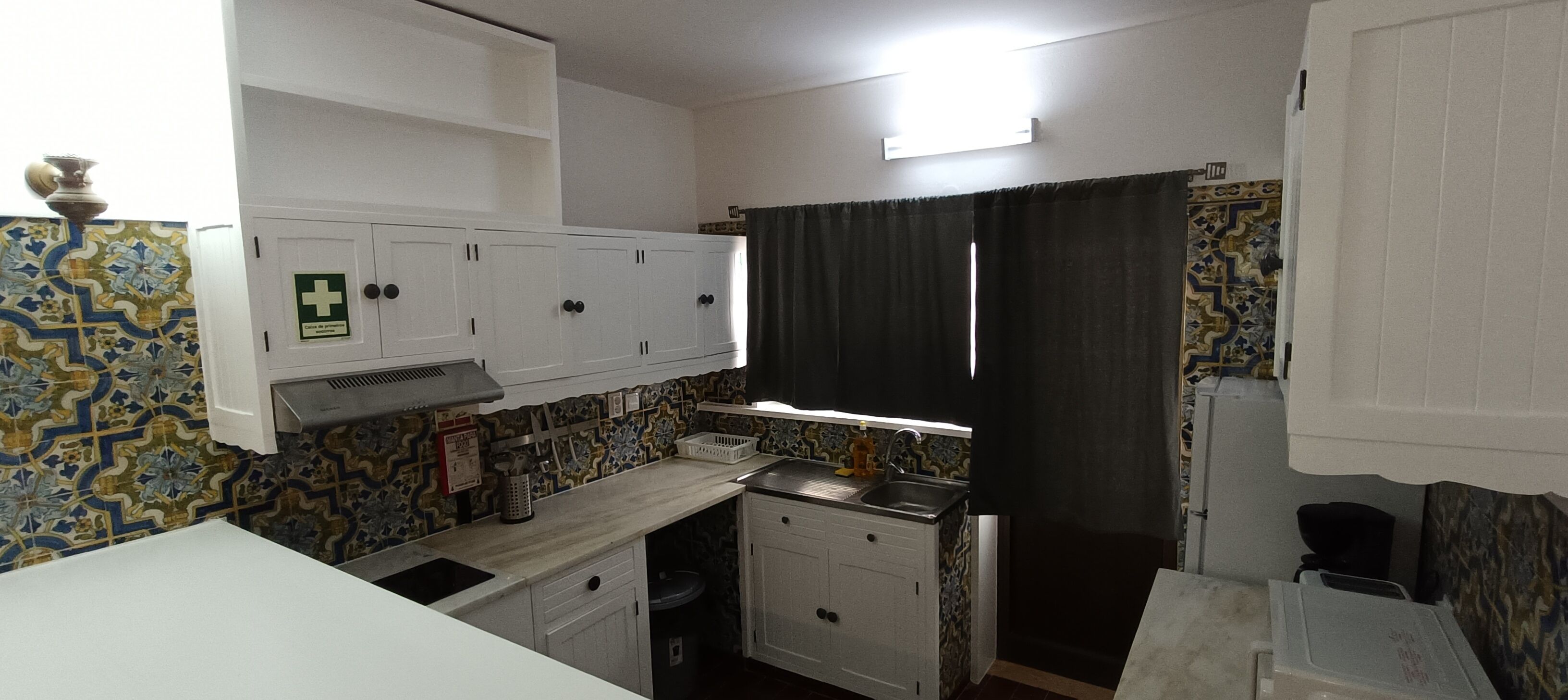 Uma cozinha compacta com armários brancos, uma pia e uma janela com cortina.