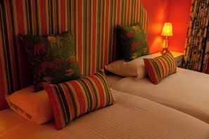 Quarto de hotel com cortinas listradas, duas camas com almofadas listradas e uma luminária sobre uma das camas.
