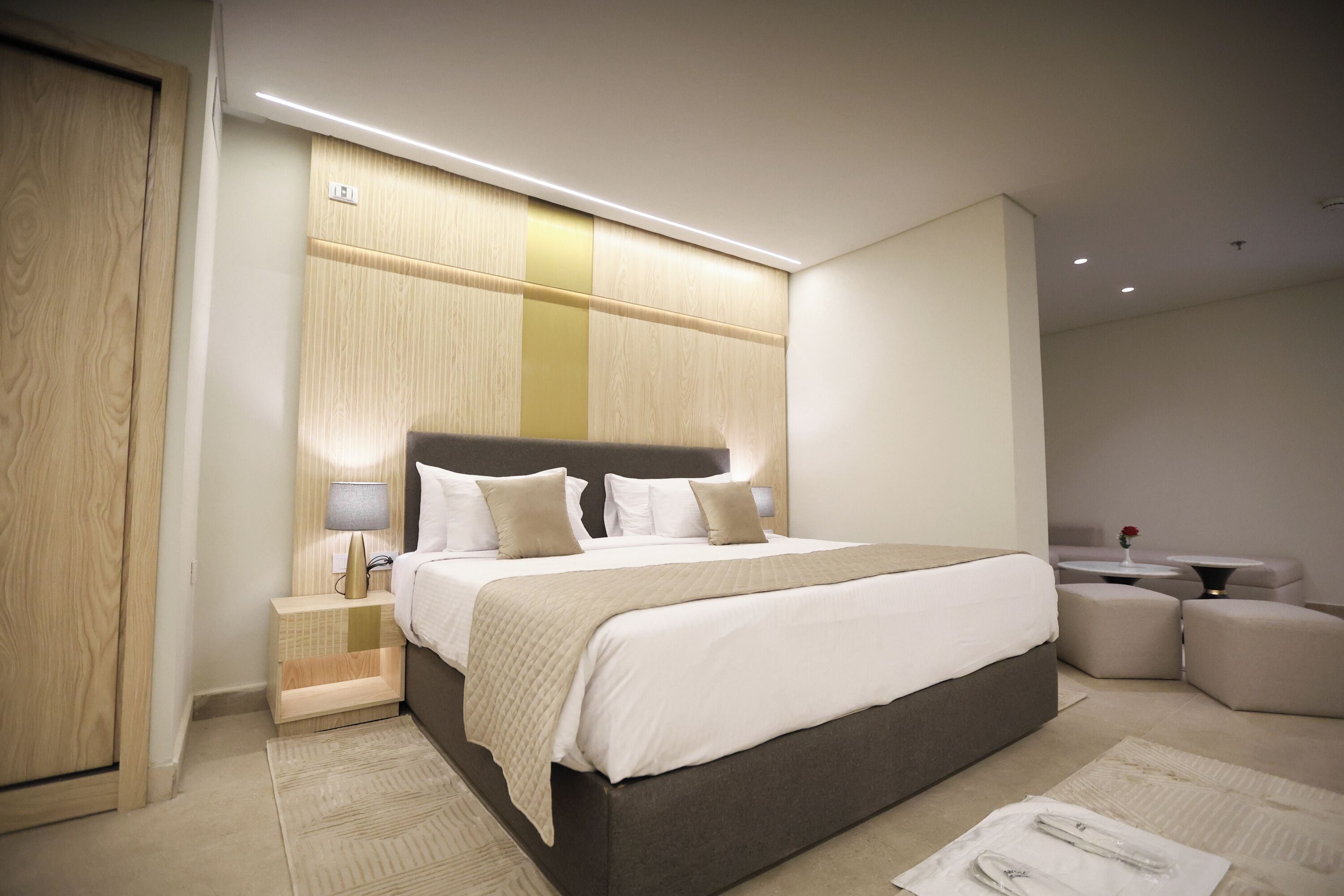 Quarto de hotel moderno com uma cama grande, mesas de cabeceira, um criado-mudo, uma luminária e uma pequena mesa com um vaso.