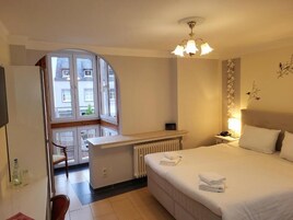 Quarto de hotel com cama, escrivaninha, cadeira, radiador, janela e lustre.