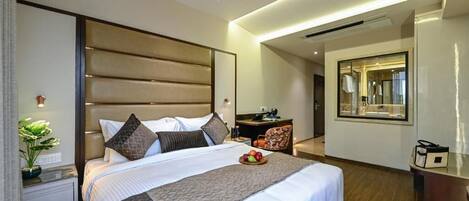 Quarto de hotel moderno com uma cama grande, uma escrivaninha, uma cadeira e um espelho.