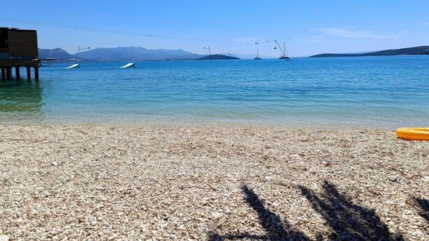 Uma praia de pedras com água cristalina, barcos e uma estrutura de madeira.