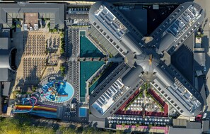Vista aérea de um hotel com piscina, espreguiçadeiras e um tobogã.