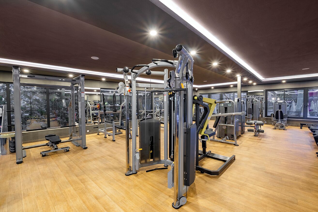 Uma academia com diversos aparelhos de exercício, amplas janelas e piso de madeira.