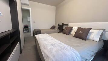 Quarto de hotel com uma cama grande, uma mesa de cabeceira, um guarda-roupa e um banheiro visível por uma porta aberta.