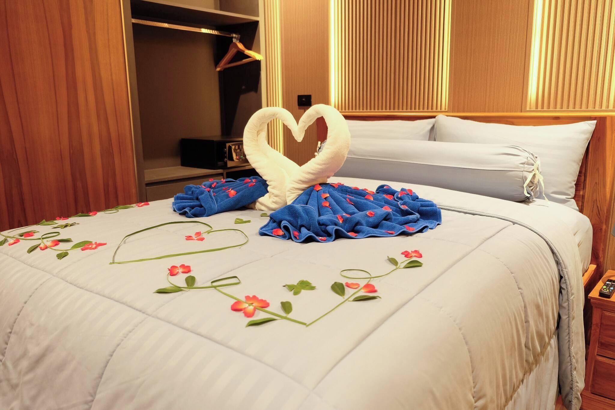 Cama bem arrumada com uma toalha em formato de coração e outra toalha azul com flores vermelhas.