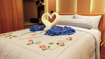 Cama bem arrumada com uma toalha em formato de coração e outra toalha azul com flores vermelhas.