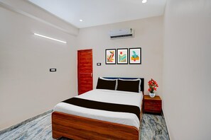 Quarto com cama, mesa de cabeceira, vaso com flores e três quadros na parede.