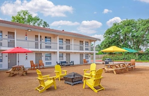 Um motel com estrutura em dois andares, área externa com assentos, cadeiras e mesas, e uma lareira.