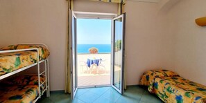 Quarto com beliches, uma porta de correr que dá para uma varanda com mesa e cadeiras, e vista para o mar.