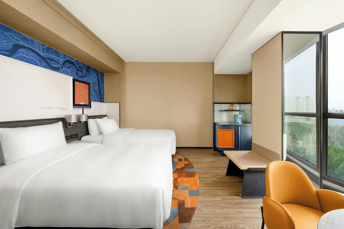 Quarto de hotel com uma cama grande, uma mesa, uma cadeira e vista para a cidade.